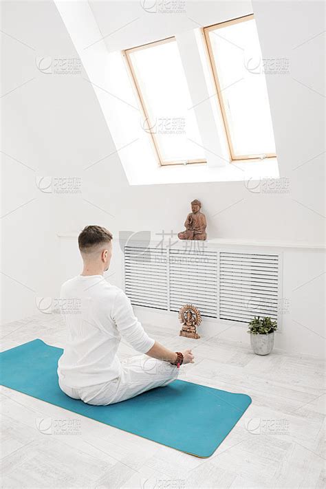 一个穿着白色裤子赤裸上身的男人在做运动瑜伽体式和伸展和冥想的姿势在明亮的体育课的背景下