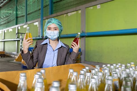 음료 공장에서 제품을 비축하기 위해 바질 씨 음료를 들고 안전 모자와 의료 마스크를 착용한 초상화 젊은 여성 매니저 25 29