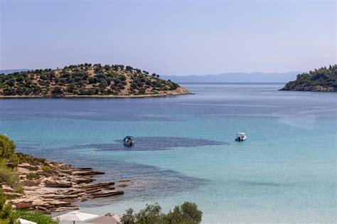 두 개의 모터 보트가 맑은 청록색 얕은 물 해안 근처의 난쟁이 나무로 덮인 작은 섬 Kalogria 흐릿한 배경의 아토스 반도 그리스로 만에 정박되어 있습니다 0명에 대한