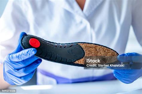 의료용 고무 장갑을 낀 의사는 평발의 치료와 예방을 위해 정형 외과 깔창을 들고 있습니다 발 관리 및 편안한 착용 신발 개선에
