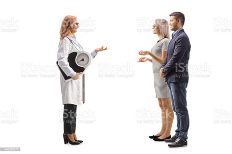 체중계를 들고 하얀 배경에 고립된 젊은 부부와 이야기하는 여성 의사의 전체 길이 프로필 샷 서 있기에 대한 스톡 사진 및 기타