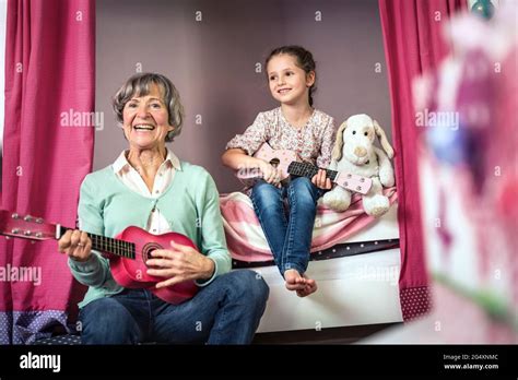Smiling Grandmother And Granddaughter With Guitar Sitting In Bedroom