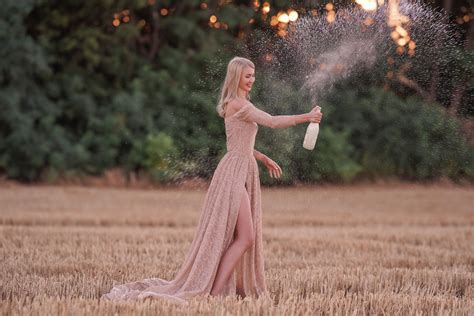 Обои на рабочий стол Девушка в длинном платье с бутылкой шампанского в руке стоит на поле