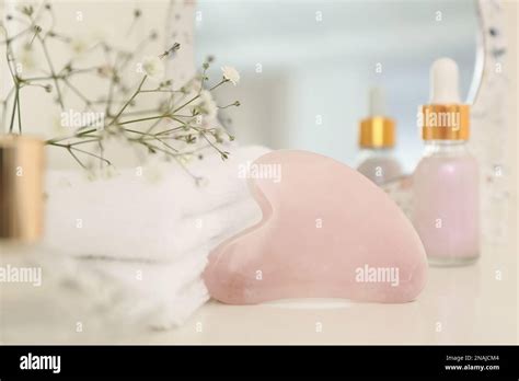 Rose Quartz Gua Sha Tool Skin Care Product And Flowers On White Table