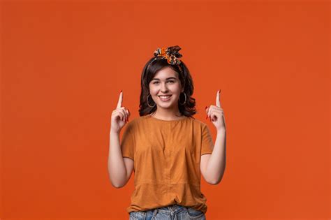 예쁜 갈색 머리 여자 에 티셔츠와 아름 다운 머리띠 가리키는 그녀의 손가락으로 오렌지 배경 위에 고립 된 광고를 위한 장소입니다 T 셔츠에 대한 스톡 사진 및 기타 이미지