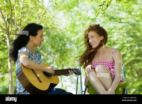 Two Young Women Sitting Outdoors One Playing Acoustic Guitar Stock