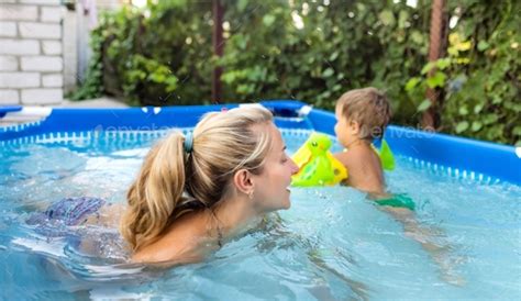Mom Plays With A Naked Baby In Oversleeves In The Pool Against The Background Of A Summer Sunset