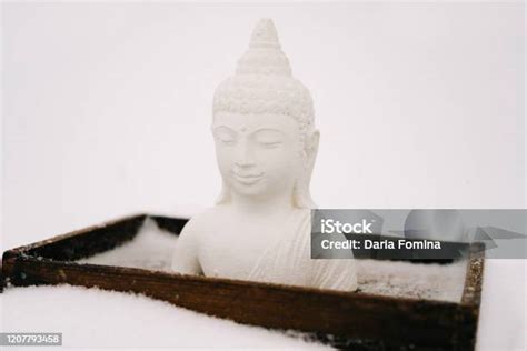 겨울에 눈이 내리는 동안 흰 눈으로 덮인 나무 스탠드에 석고로 만든 흰색 부처님의 작은 동상 0명에 대한 스톡 사진 및 기타