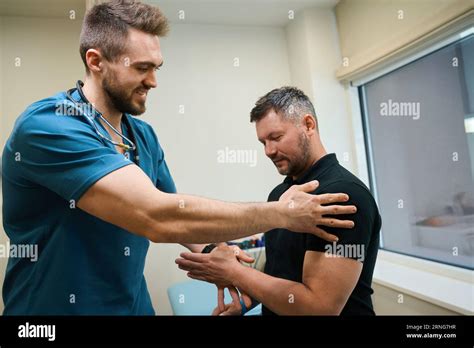 Man Sitting On Examination Couch While Physical Therapist Assessing His Arm Muscle Tone During