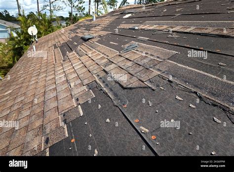 Wind Damaged House Roof With Missing Asphalt Shingles After Hurricane