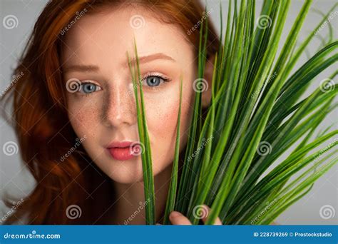 Ginger Haired Young Female Looking At Camera Through Plant Gray