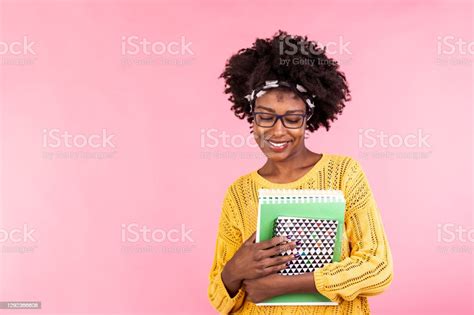 분홍색 배경 초상화에 손으로 고립 된 책을 들고 안경을 쓴 젊은 여학생 미소 짓는 노트북을 들고 있는 캐주얼한 일상 생활 양식
