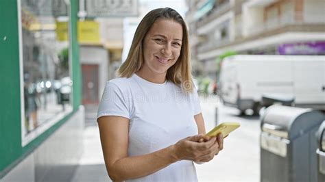 beautiful blonde adult woman happily using her smartphone outdoors