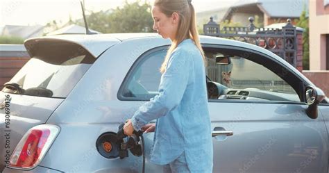 Close Up Woman Plugs In Charger Into Socket Of Her Modern New Electric Car Girl In A Casual