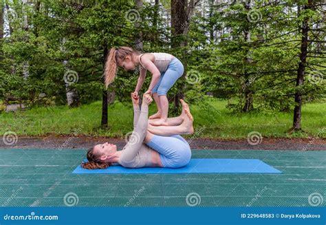 Mother And Daughter Doing Yoga On Grass In The Park At The Daytime