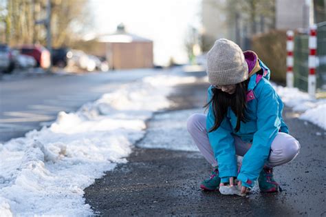 안경 모자 겨울 재킷을 입은 슬픈 십대 소녀가 바깥 아스팔트에서 얼음 조각을 가지고 놀고 있습니다 어린이의 야외 활동의 개념 8 9 살에 대한 스톡 사진 및 기타 이미지