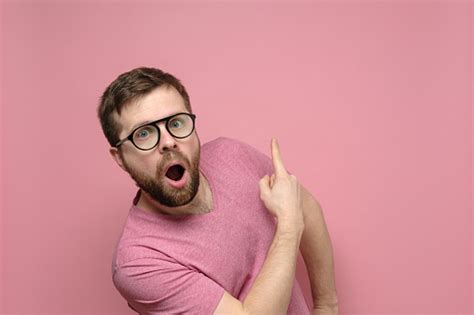 놀란 남자는 집안의 사본을 검지 손가락으로 가리키고 분홍색 배경에 입을 벌리고 카메라를 봅니다 가리키기에 대한 스톡 사진 및