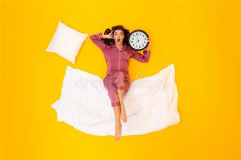 Shocked Lady Holding Alarm Clock Lying On Yellow Background Stock Image
