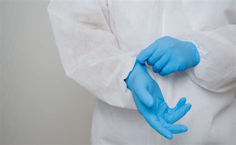 흰색 배경에 고립 된 그의 손에 파란색 장갑을 검사 Ppe 정장에 넣어 바이러스 학자의 초상화를 닫습니다 개인 보호 장비 개념