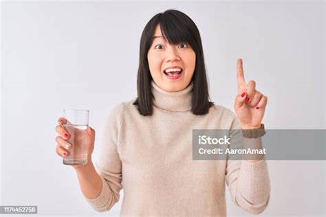젊은 아름다운 중국 여자 들고 유리 의 물 위에 고립 된 흰색 배경 놀란 에이 아이디어 또는 질문 가리키는 손가락 으로 행복한
