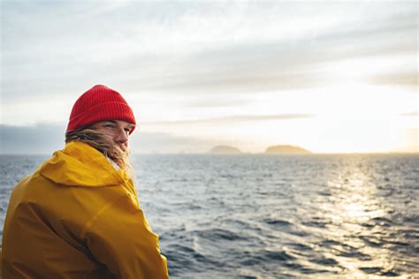노란 비옷과 빨간 모자를 쓰고 일몰 바다와 안개가 자욱한 산을 바라보는 혼자 여행자 라이프 스타일 아웃 도어 어드벤처