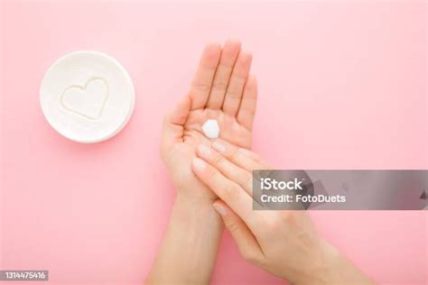 젊은 성인 여성 손 화이트 크림을 사용 하 여 밝은 분홍색 테이블 배경에 하트 모양의 항아리 파스텔 색상 깨끗하고 부드러운 바디 스킨에 신경을 쓰다 근접 촬영 관점 샷 하향