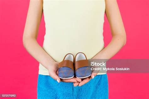 분홍색 배경에서 그녀의 배에 대한 아기 소년을위한 부츠를 들고 화려한 가정 의류에 임신 한 여성의 자른 이미지 행복한 임신 복사