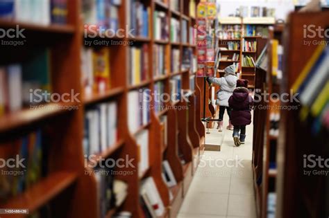 재킷을 입은 여동생들이 도서관의 책장에서 책을 꺼내고 있다 유럽 아이들의 학습과 교육 도서관에 대한 스톡 사진 및 기타 이미지 도서관 아기 읽기 Istock