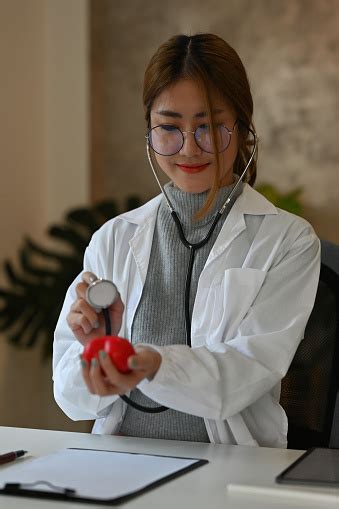 하얀 코트를 입은 예쁜 아시아 의사가 사무실에 앉아 자신감 넘치는 미소로 심장 모델을 들고 청진기로 검진 포즈를 취하는 초상화 의료 및 건강 관리 개념 25 29세에 대한