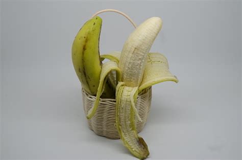 반쯤 껍질을 벗긴 바나나 하나와 껍질을 벗기지 않은 잘 익은 녹색 바나나 1개는 흰색 배경에 격리된 등나무 바구니에 담겨
