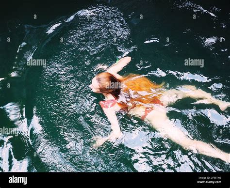 Une jeune fille à poil long dans un bikini orange se baignait dans un turquoise foncé rivière