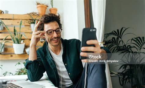 집에서 원격으로 작업하는 노트북과 스마트 폰을 가진 남자는 휴대 전화로 화상 통화를합니다 원격 작업에서 프리랜서 아늑한 직장