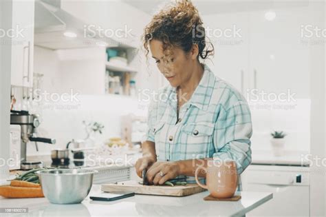 한 젊은 성인 여성이 집에서 혼자 부엌에서 샐러드나 다이어트 점심을 위해 야채를 준비하고 있다 실내 배경에 있는 흰색 현대 부엌