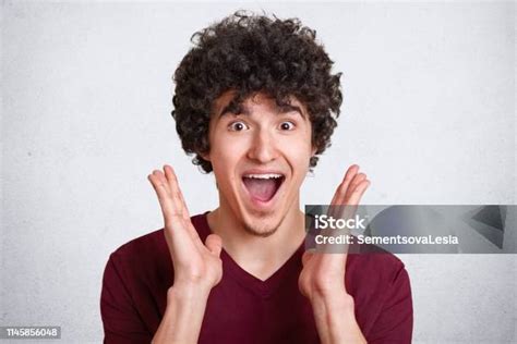 어두운 곱슬 머리와 매력적인 남자의 스튜디오 촬영 입을 열어 유지 뭔가 비명 만족 얼굴 표정으로 스탠드 높은 정신을가지고 그의