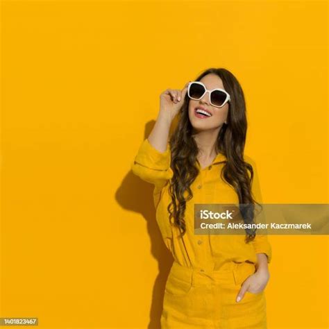 린넨 셔츠와 반바지를 입은 젊은 여성이 선글라스를 입고 노란 벽에 포즈를 취하고 있습니다 사람들에 대한 스톡 사진 및 기타