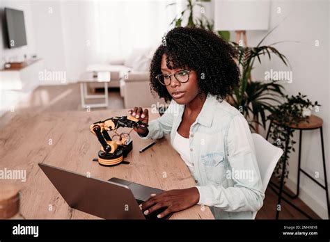 Engineer Using Laptop Holding Robot Model At Desk In Home Office Stock