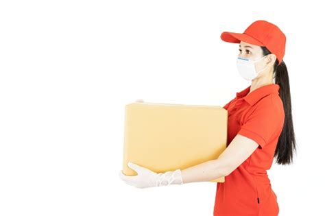 흰색 배경에 고립 된 마스크를 입고 빨간 유니폼을 입은 배달 여성 모자 티셔츠 청바지 택배 또는 골판지 상자를 들고 딜러로
