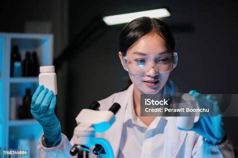 Asian Female Scientist Looking Under Microscope Analyzes Petri Dish