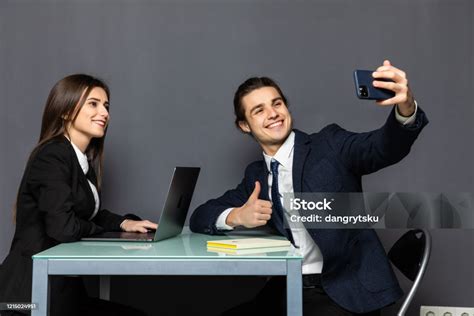 젊은 비즈니스 동료 부부는 흰색 벽 배경 위에 고립 된 테이블에 앉아 휴대 전화로 셀카를 찍습니다 경영자에 대한 스톡 사진 및 기타 이미지 Istock