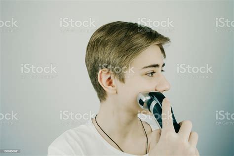 흰색 티셔츠를 입은 잘생긴 미소 짓는 십대의 초상화가 처음으로 수염과 수염을 전기 면도기로 면도합니다 16 17 살에 대한 스톡