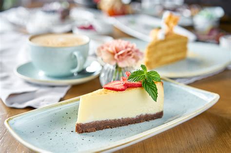 흰 접시에 딸기와 민트 잎을 곁들인 맛있는 치즈 케이크 조각 카페에서 아침 식사 모닝 커피 카푸치노와 테이블에 디저트를 많이