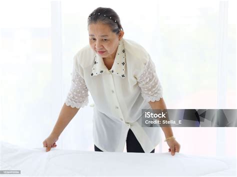 행복한 미소 아시아 노인 여성 주부 청소 및 침실에서 침대를 만들기 할머니가 집안일과 청소를하고 흰색 담요와 시트를 변경 하는