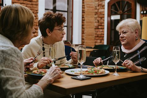 검은 색과 흰색 옷을 입은 노인 의 공정한 머리와 검은 머리 여성은 테이블에 앉아 칼과 포크로 피자를 먹고 와인이나 샴페인을