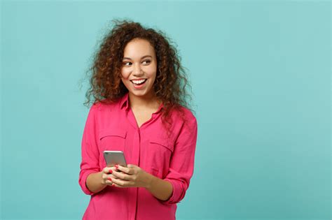 스튜디오에서 파란색 청록색 벽 배경에 고립 된 휴대 전화 입력 Sms 메시지를 사용 하 여 분홍색 캐주얼 옷에 쾌활 한 아프리카