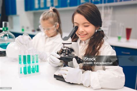 실험실 코트에서 두 작은 아이 학교 실험실에서 화학 학습 실험실 또는 화학 내각에 있는 실험을 만드는 방어적 인 유리에 있는 젊은 과학자 현미경을 통해 보고 Stem 주제에