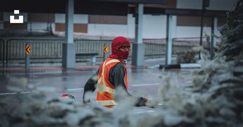 주황색과 검은색 재킷과 빨간 니트 모자를 쓴 남자가 젖은 땅에 서 있다 사진 Unsplash의 무료 사람의 이미지