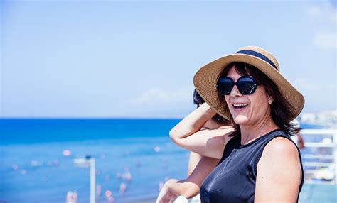 밀짚모자를 들고 카메라를 바라보는 선글라스를 쓴 중년 여성 해변을 배경으로 공간을 복사한다 50 54세에 대한 스톡 사진 및