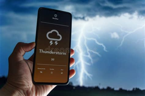Hand Holding A Smartphone Displaying A Weather App With A Thunderstorm