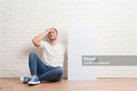 흰색 벽돌 벽 머리에 손으로 압박 물의 병을 들고 앉아 젊은 백인 남자 충격 수치심과 깜짝 얼굴로 분노와 좌절 두려워 하 고 실수에 대 한 화가 감정에 대한 스톡 사진 및