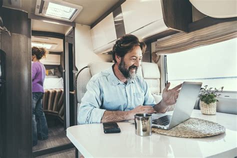 Man And Woman Living Off Grid Inside A Modern Camper Working On Laptop